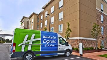 Uma van de entrega do Holiday Inn Express & Suites estacionada em frente a um edifício com fachada de tijolos e várias janelas.