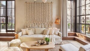 Uma sala de estar moderna com sofá, mesa de centro e elementos decorativos como um painel de macramé e luminária pendente.