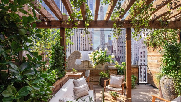 Um jardim no terraço com pérgola de madeira, área de estar e plantas em vasos.