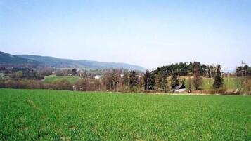Paisagem rural com um campo verde, um pequeno edifício e colinas ao longe.