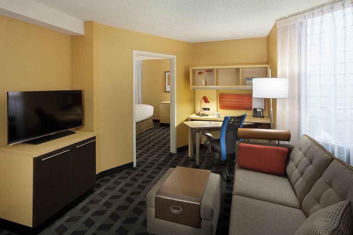 Quarto de hotel com televisão, sofá, secretária e cama.