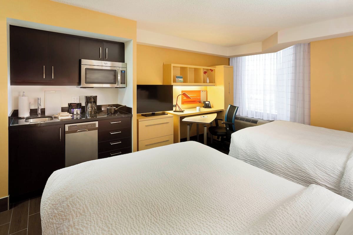Quarto de hotel com cozinha compacta, cama, escrivaninha e janela com cortinas.