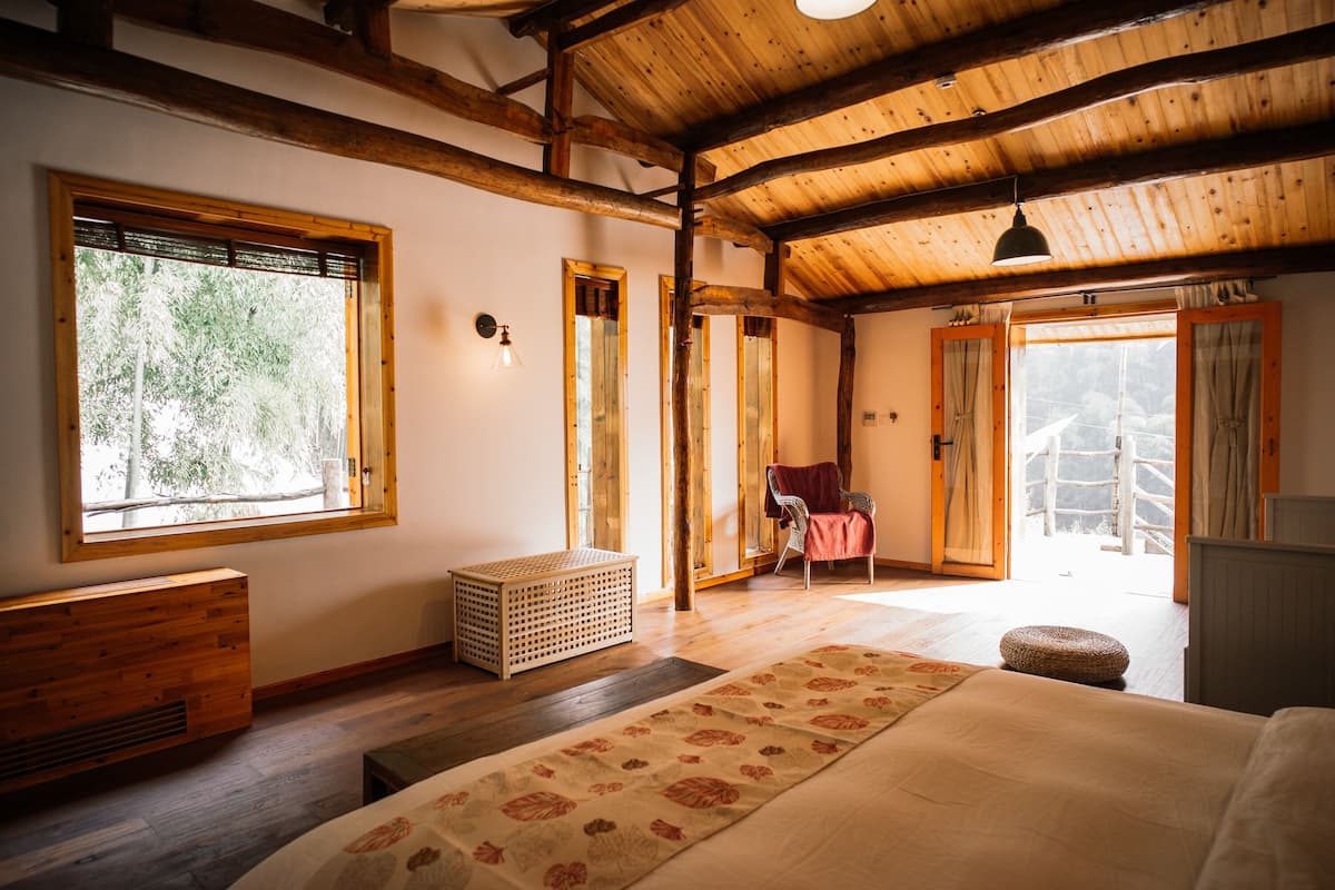 Quarto espaçoso com teto de madeira, janelas amplas, uma cama, uma cadeira e um radiador.