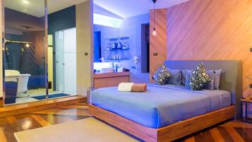 Quarto moderno com cama grande, piso de madeira, área de chuveiro com vidro e cozinha planejada com prateleiras.