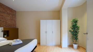 Quarto de hotel moderno com cama, guarda-roupa, planta em vaso e parede de tijolos.