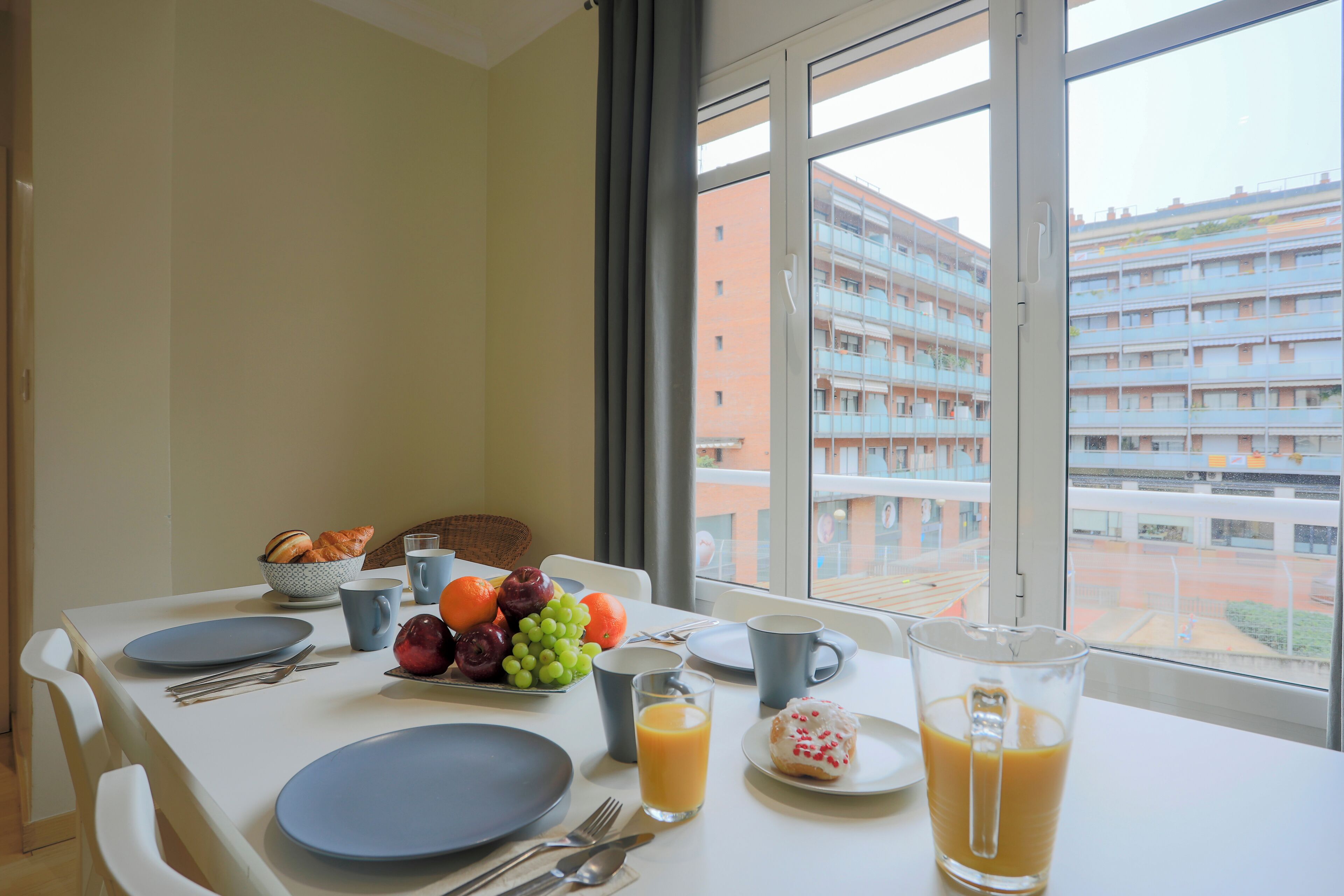 Uma mesa de café da manhã com pratos, talheres, uma tigela de frutas e um copo de suco de laranja.