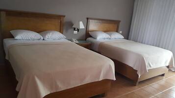 Duas camas de solteiro com cabeceiras de madeira, roupa de cama branca, mesa de cabeceira com abajur e telefone.