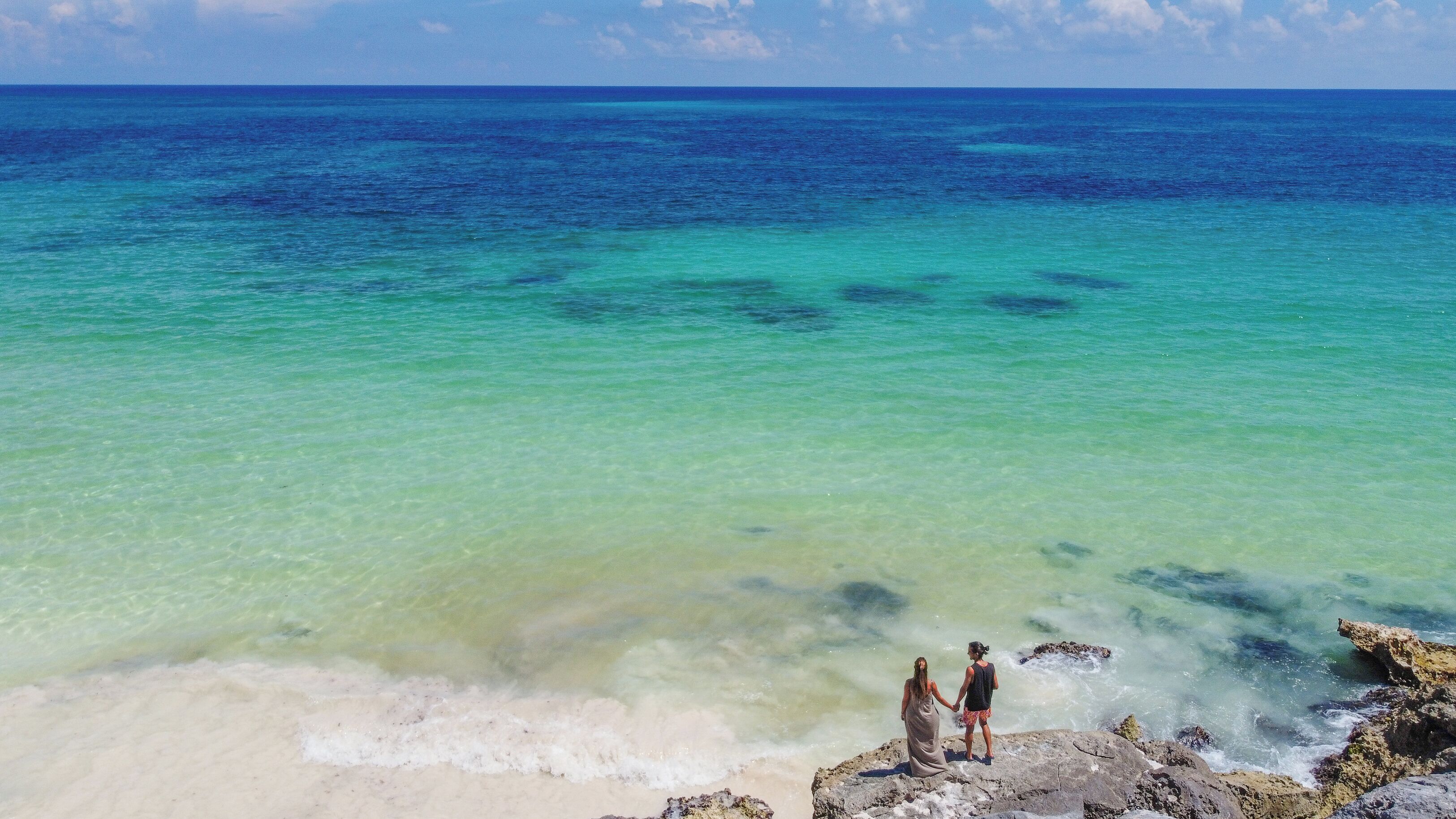 Uma praia com águas turquesa cristalinas e afloramentos rochosos.