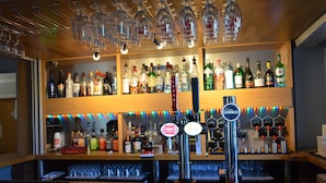 Uma área de bar com prateleiras cheias de garrafas de bebidas variadas, uma torneira com a inscrição 'Guinness' e um letreiro 'Carling'.