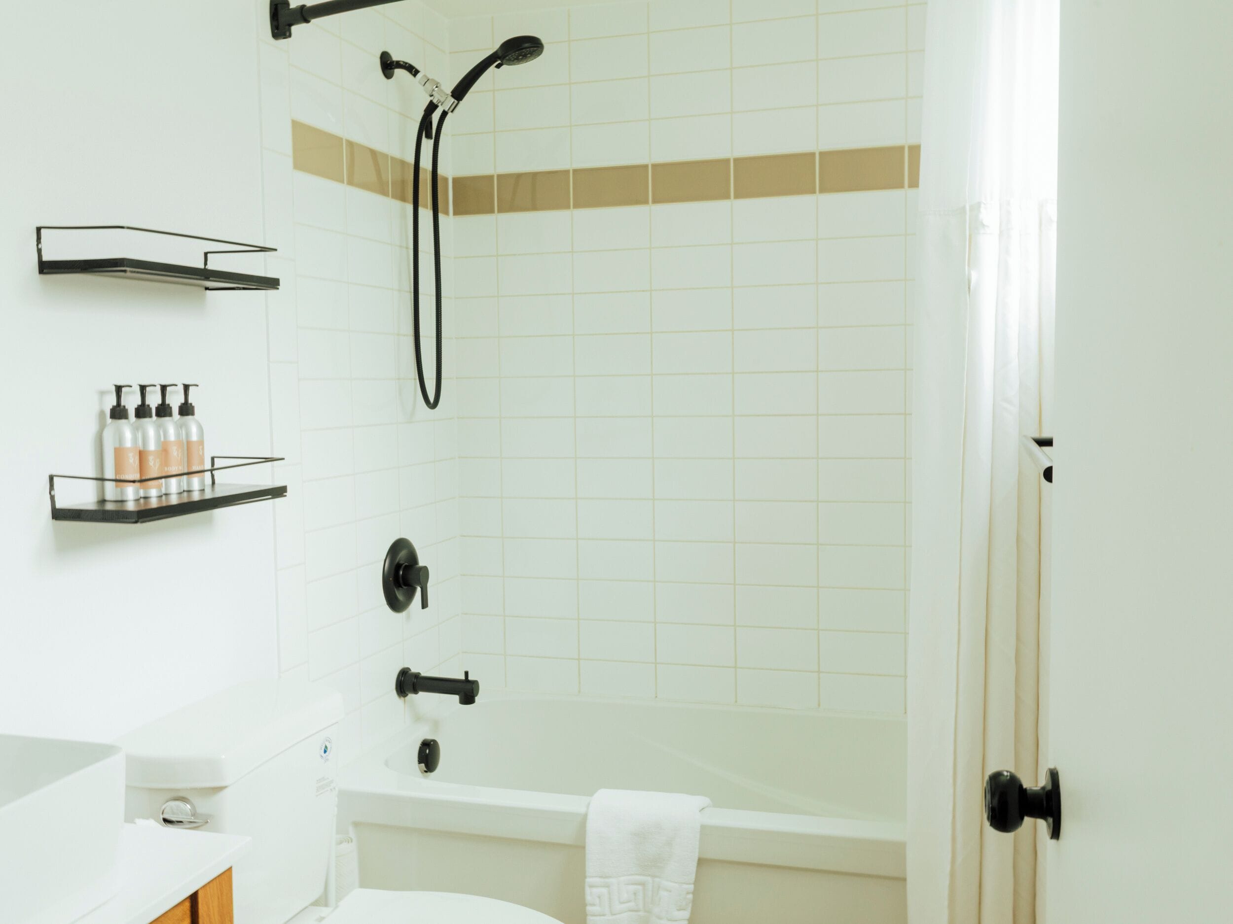 Casa de banho moderna com banheira, sanita e chuveiro. Existem prateleiras com produtos de higiene e uma toalha pendurada na parede.