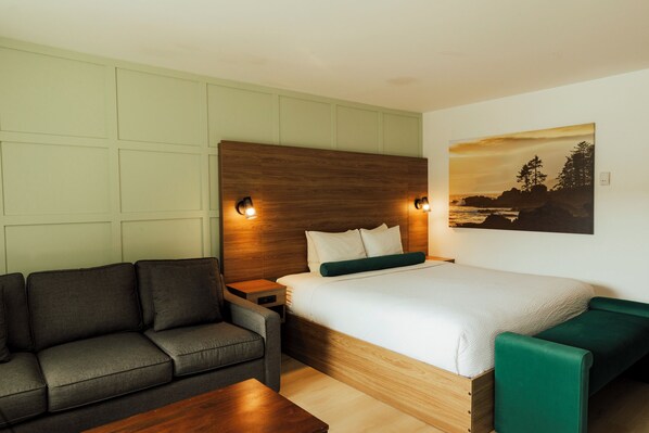Quarto moderno com cabeceira de madeira, cama com roupa de cama branca, poltrona verde, sofá cinza e mesa de cabeceira de madeira.