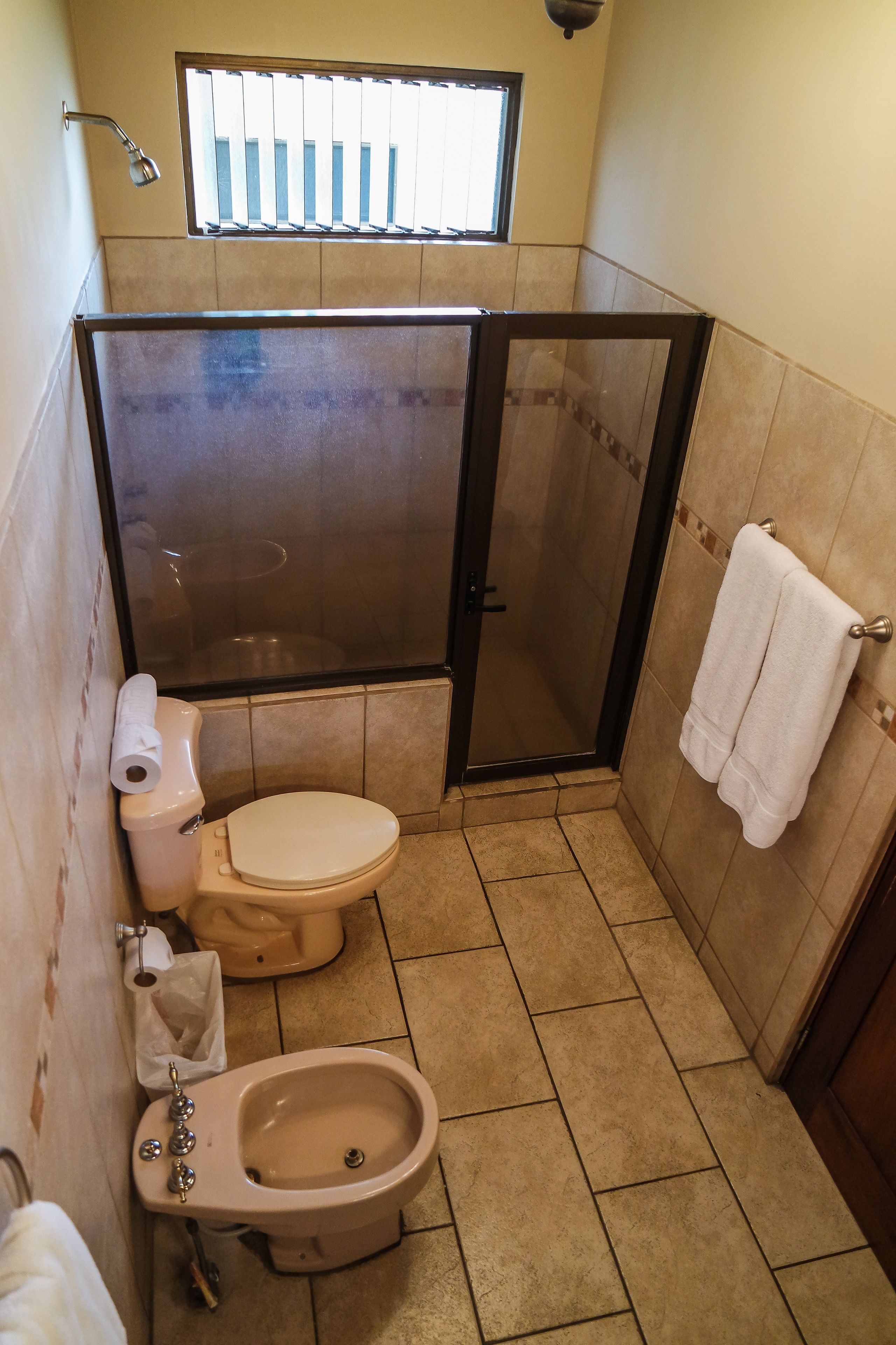 Casa de banho compacta com sanita, bidé e cabine de duche com vidro.