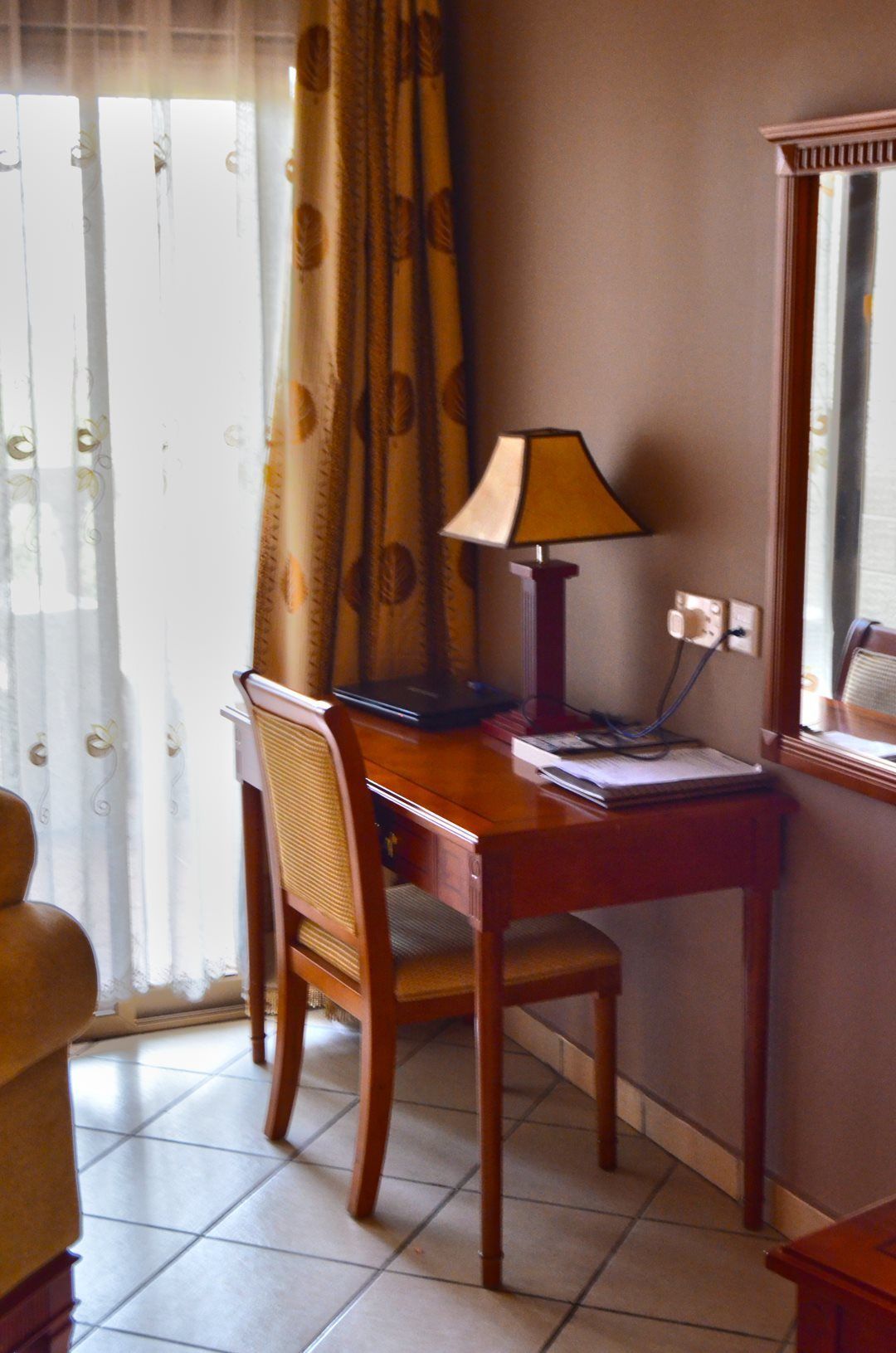 Um quarto com uma escrivaninha de madeira, um laptop, uma luminária e uma cadeira.