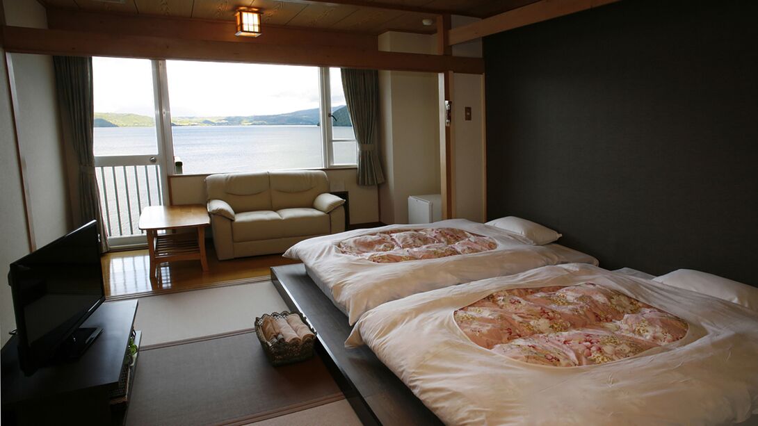 Quarto de hotel com duas camas, um sofá, uma televisão e vista para o mar.