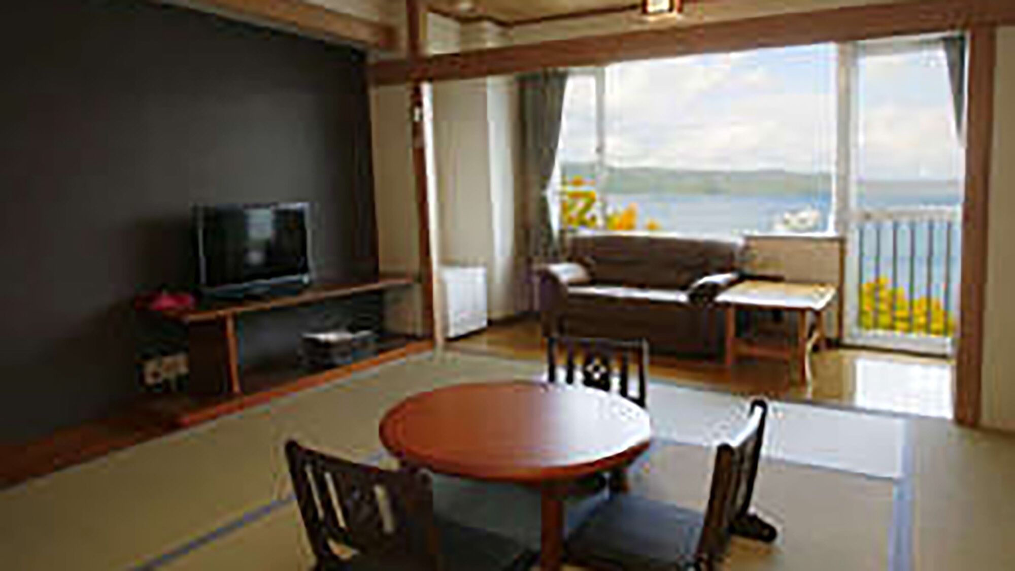 Uma sala de estar com televisão, sofá, mesa e cadeiras.