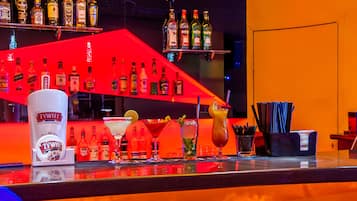 Uma área de bar com diversas garrafas de bebidas, um recipiente grande com a marca ZYWIEC e vários copos de cocktail.