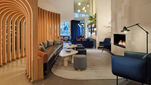 Uma área de lounge moderna com disposição de assentos curvada, lareira e vista panorâmica da cidade através de grandes janelas.