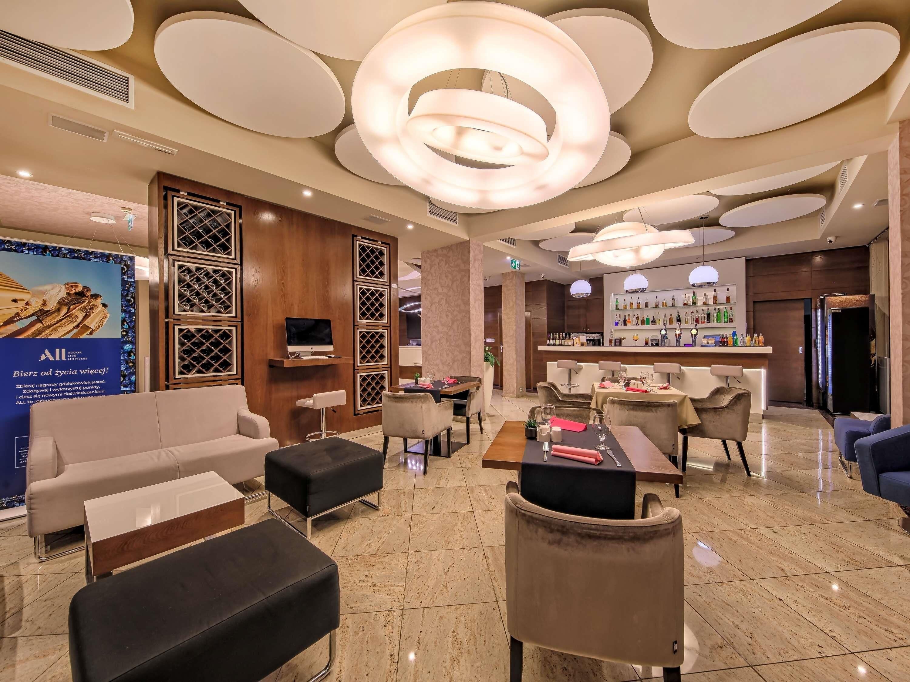 Um lobby de hotel moderno com área de bar, espaços de estar e um grande anúncio na parede.