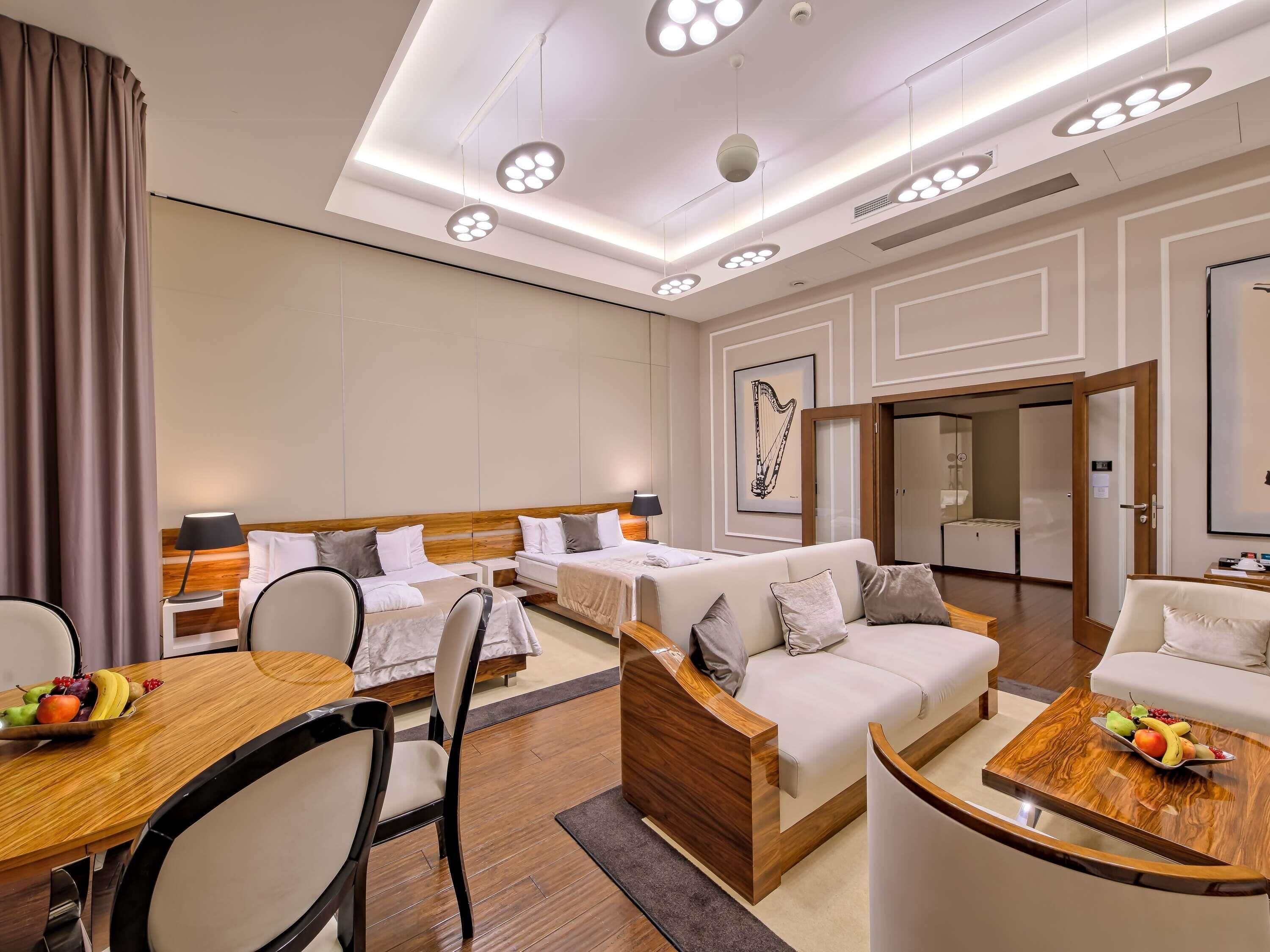 Quarto de hotel com duas camas, um sofá, uma mesa de jantar com frutas e um espelho grande.