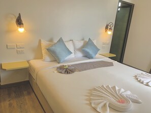 Cama bem arrumada com toalha e almofada decorativa, mesa de cabeceira com abajur e espelho na parede.