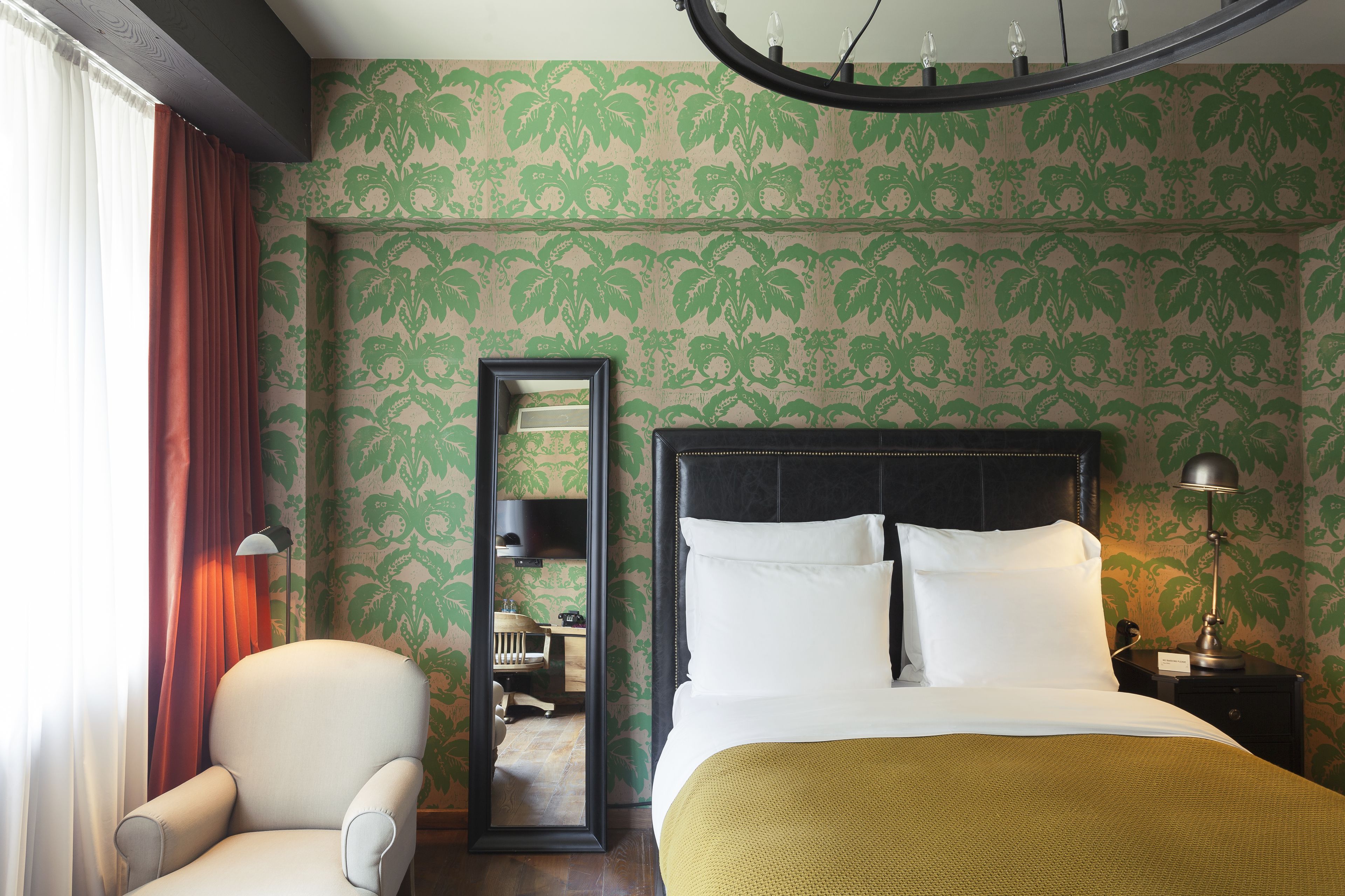 Quarto de hotel com uma cama, uma cadeira, uma mesa de cabeceira, um abajur e um espelho.