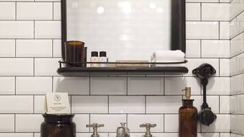 Um banheiro com parede de azulejos brancos, um espelho, uma prateleira com produtos de higiene pessoal, uma toalha e um dosador de sabonete líquido.