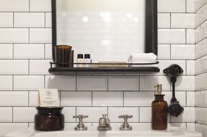 Um banheiro com parede de azulejos brancos, um espelho, uma prateleira com produtos de higiene pessoal, uma toalha e um dosador de sabonete líquido.