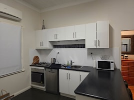 Cozinha compacta com armários brancos, bancada preta, lava-louças em aço inoxidável, fogão a gás e micro-ondas.