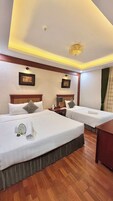 Quarto de hotel com duas camas, piso de madeira, lustre e quadros nas paredes.