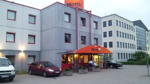 Um motel com toldo vermelho, um carro estacionado em frente e um edifício com várias janelas.