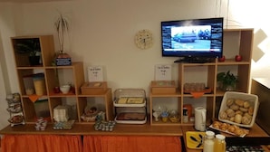 Um balcão de café da manhã com chá, café, lanches e uma televisão exibindo um noticiário.