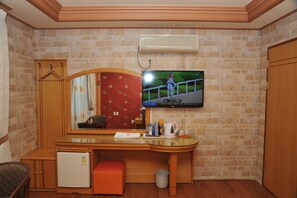 Quarto de hotel com parede de tijolos, penteadeira de madeira com espelho, televisão na parede, pequeno frigorífico e lixeira.