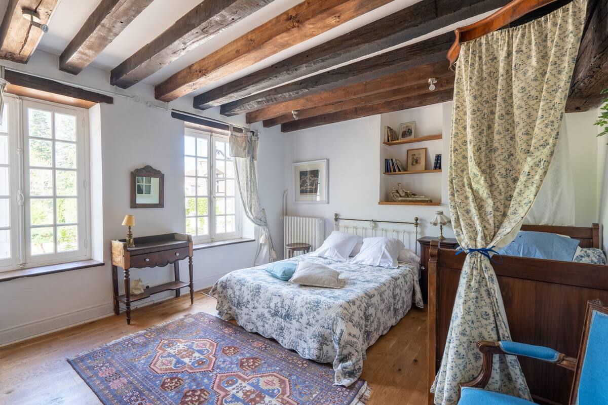Quarto com teto de madeira, cama com colcha florida, cadeira azul e tapete estampado.