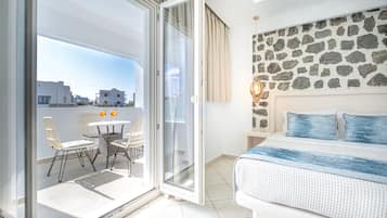 Quarto de hotel com cama, parede de pedra, varanda com cadeiras e vista para edifícios.