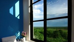 Quarto com uma grande janela com vista para uma paisagem verde, uma banheira branca e uma parede azul.
