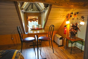 Um quarto de sótão acolhedor com uma mesa de madeira, duas cadeiras, um radiador e uma estátua decorativa.