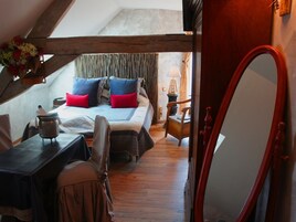 Um quarto de sótão aconchegante com teto de madeira, uma cama com muitos travesseiros, uma mesinha com uma chaleira e um espelho.