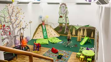 Uma sala de jogos infantil com um escorrega, tapetes de atividades e uma mesa com cadeiras.