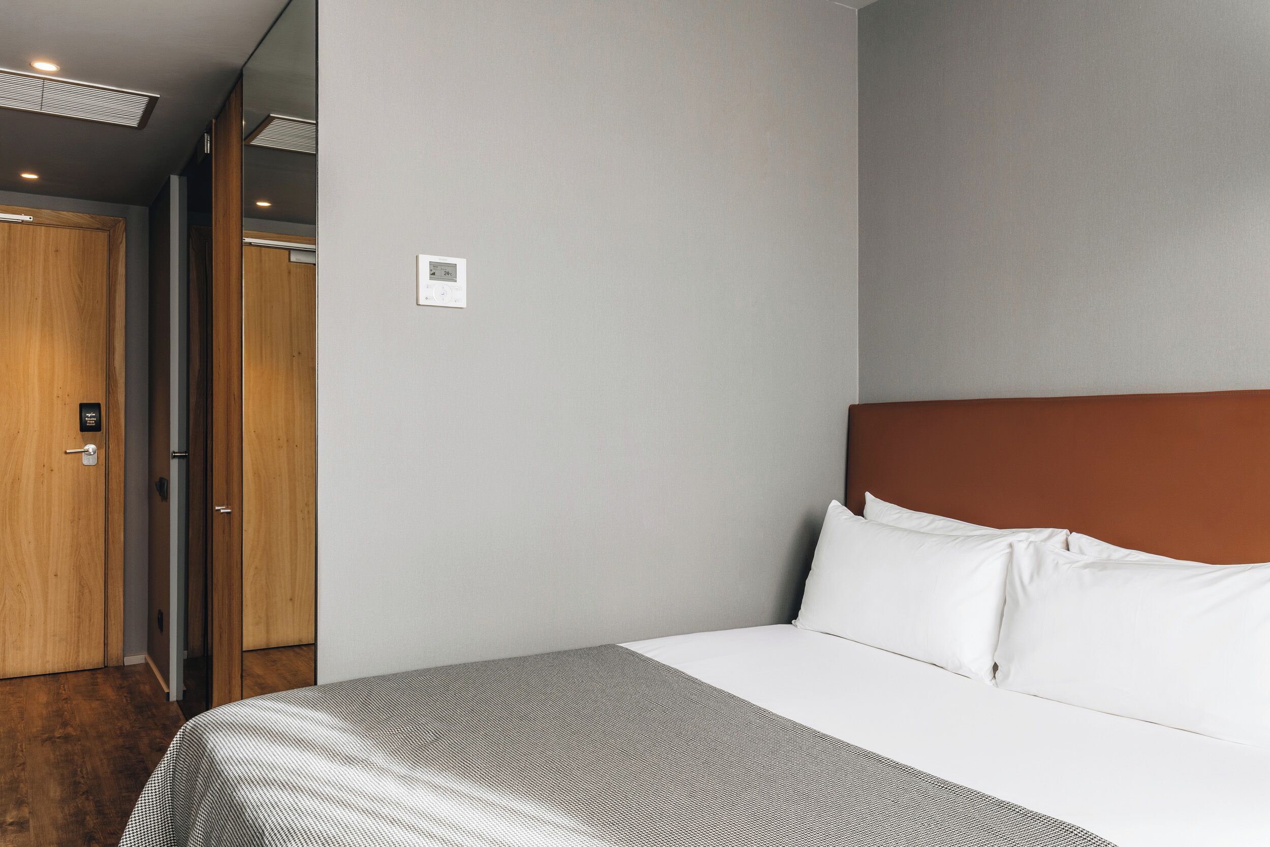 Quarto de hotel com uma cama, guarda-roupa de madeira e um termostato na parede.