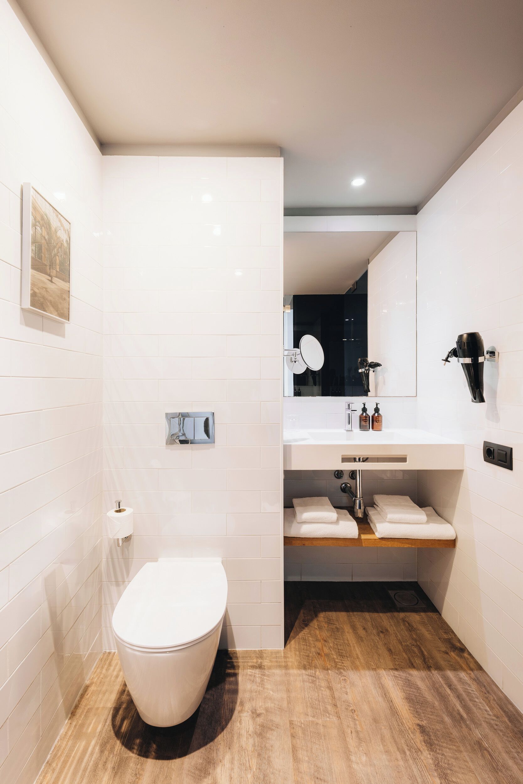 Uma casa de banho moderna com sanita branca, lavatório com espelho e secador de cabelo fixado na parede.