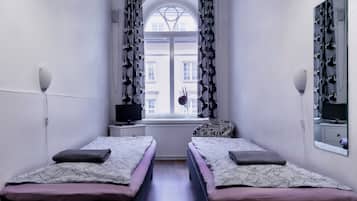 Quarto com duas camas, janela com cortinas, radiador, televisão e espelho na parede.