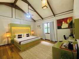 Quarto com uma cama grande, uma escrivaninha, uma cadeira, ventilador de teto e janela com cortinas.