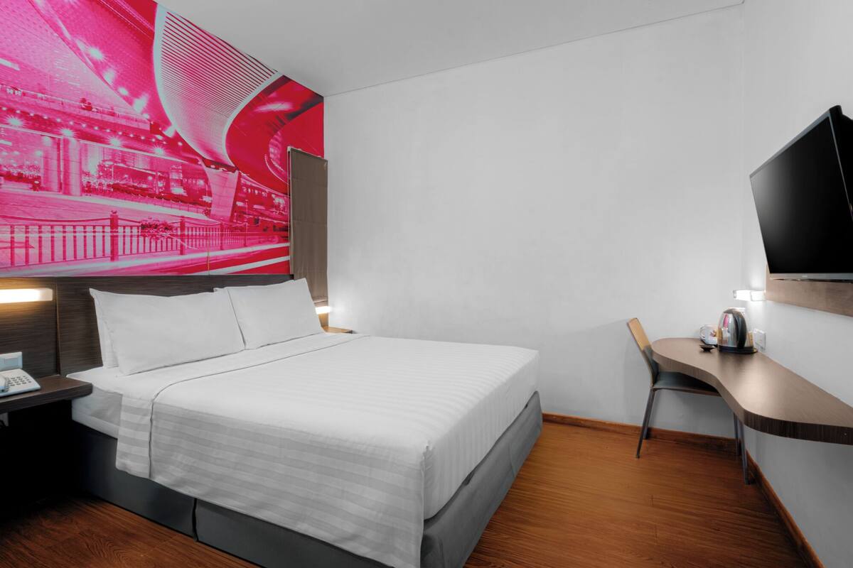 Quarto de hotel com cama, escrivaninha, cadeira, televisão e uma grande obra de arte digital na parede.