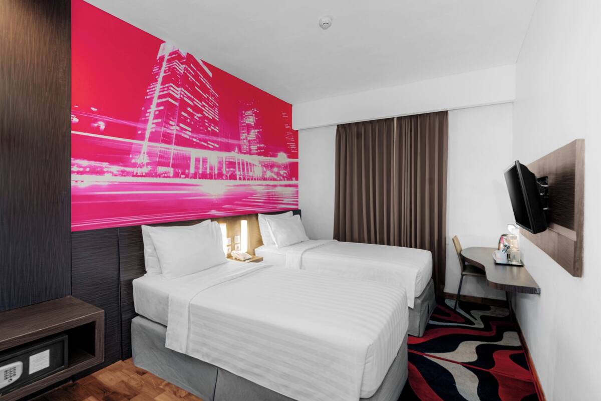 Quarto de hotel com cama, escrivaninha, televisão e uma grande tela digital exibindo uma vista urbana.