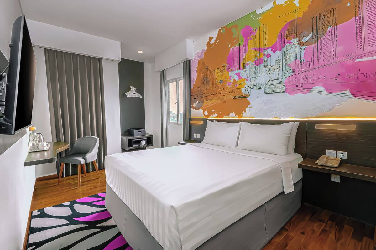 Quarto de hotel com uma cama, escrivaninha, cadeira, televisão e um mapa grande e colorido na parede.