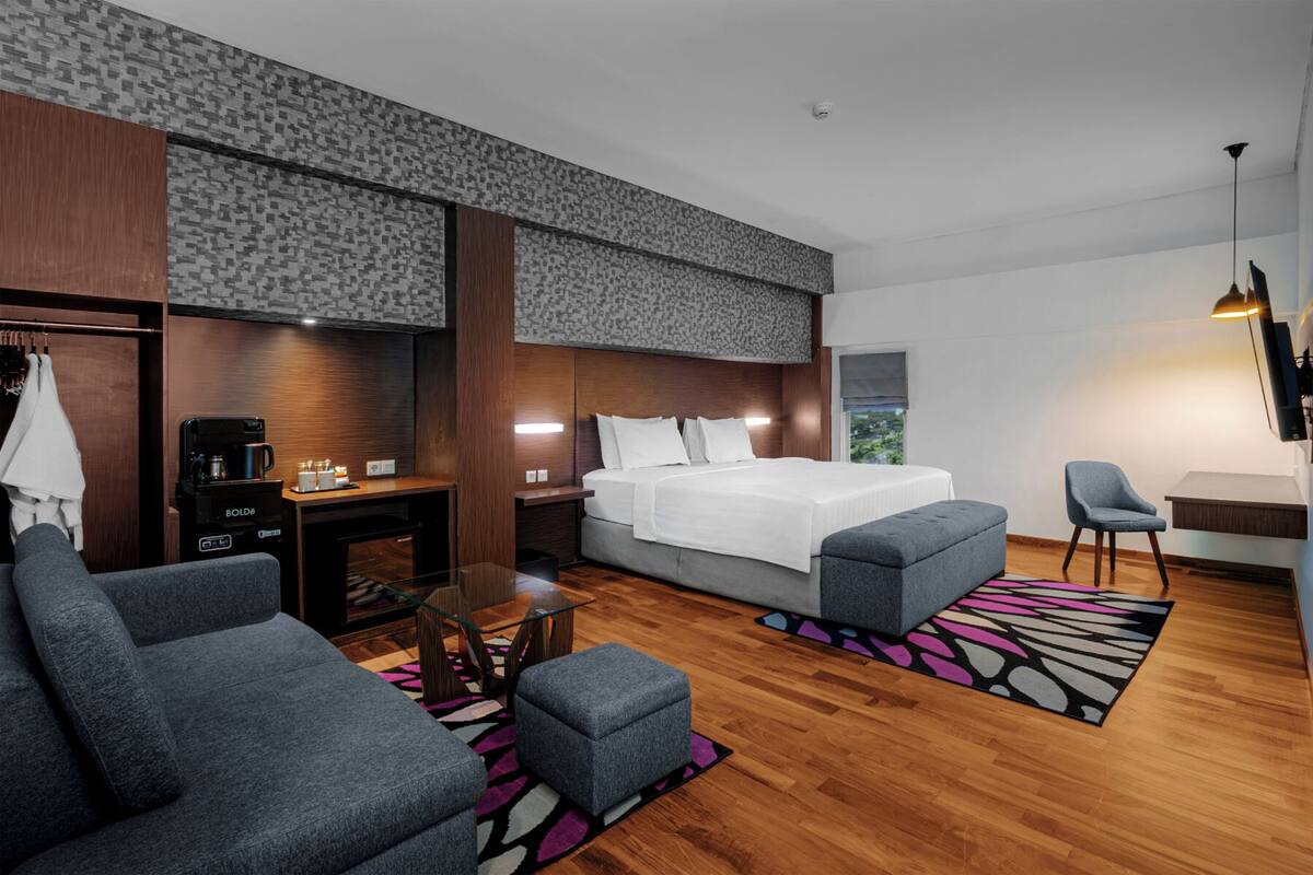 Quarto de hotel moderno com cama, área de estar, cafeteira e vista para o exterior.