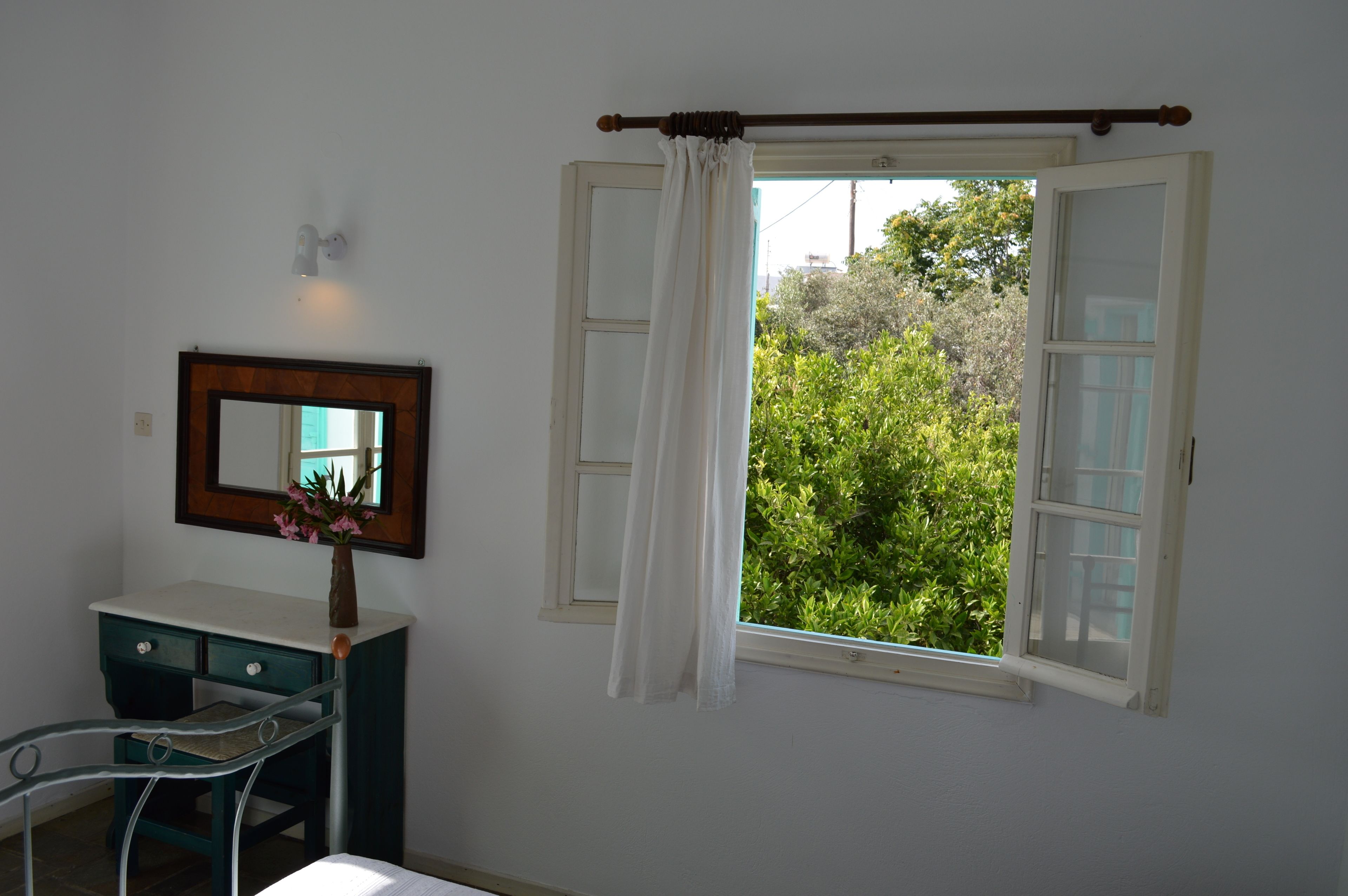 Um quarto com janela, espelho, penteadeira e cadeira.