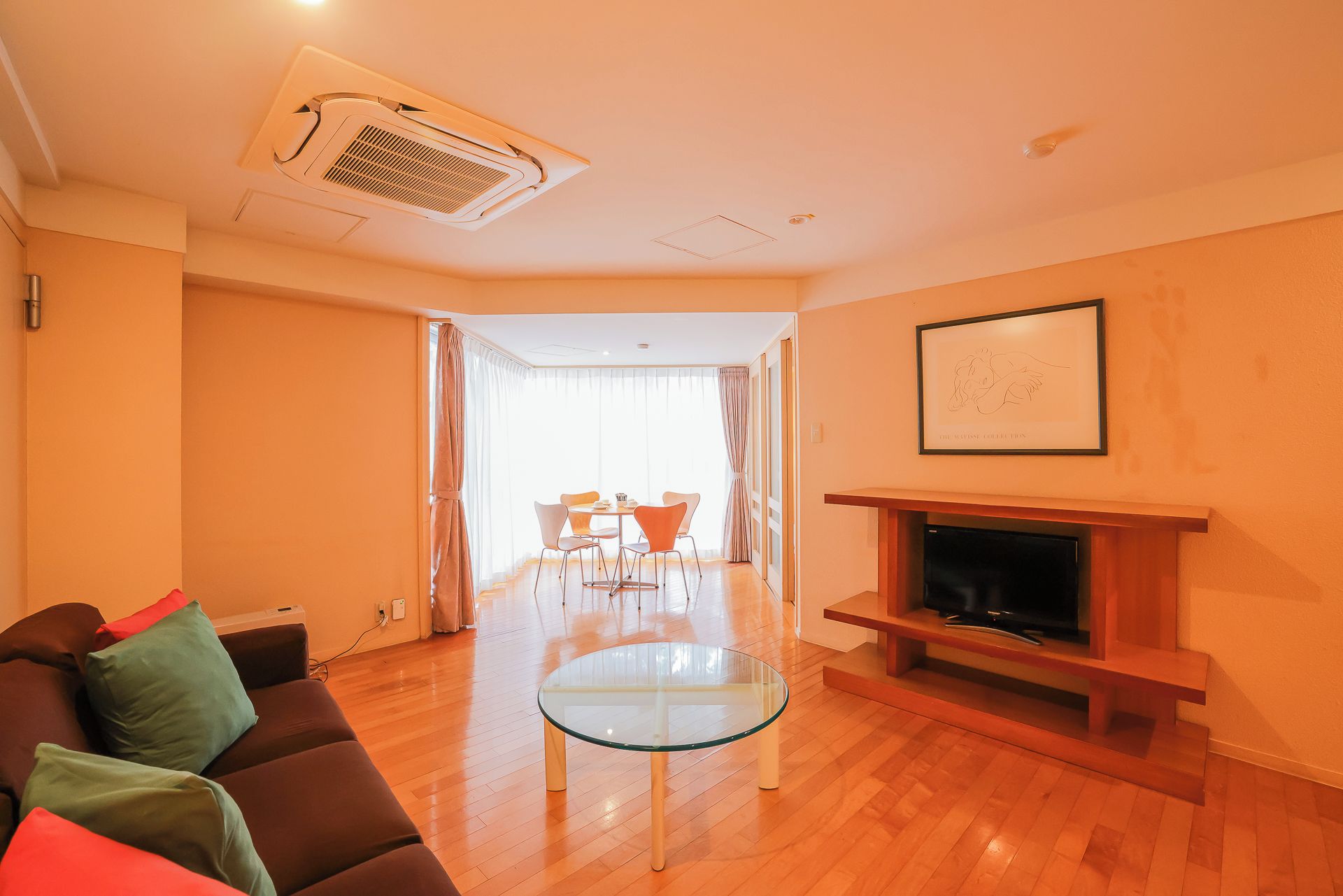 Uma sala de estar com sofá, mesa de centro de vidro, lareira e um espaço de jantar ao fundo.