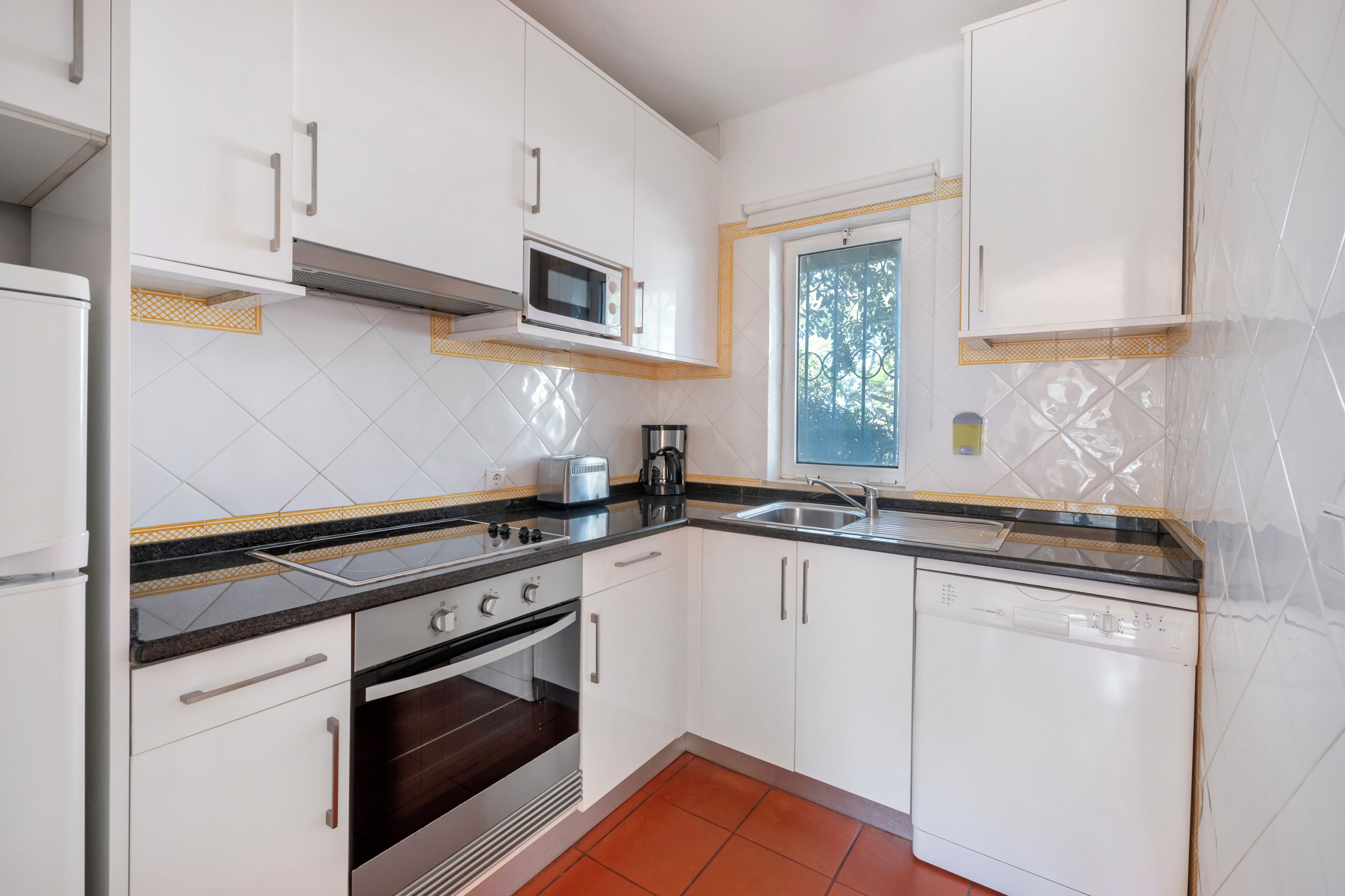 Uma cozinha moderna com armários brancos, micro-ondas, torradeira e lava-louças.