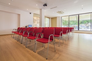 Sala de conferências com fileiras de cadeiras vermelhas, um projetor e amplas janelas com vista para o exterior.